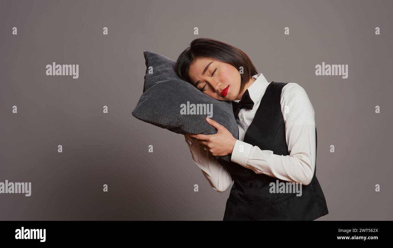 Asian front desk staff falling asleep with pillow in hand, feeling ...