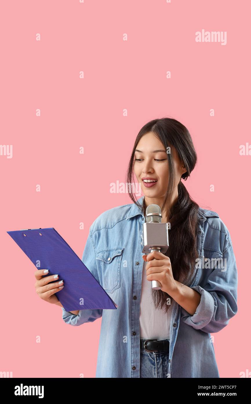 Female Asian journalist with microphone and clipboard talking on pink ...