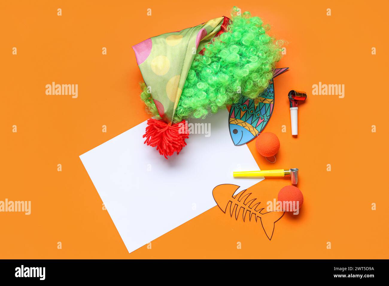 Blank card with paper fishes, clown wig and party whistles on orange ...