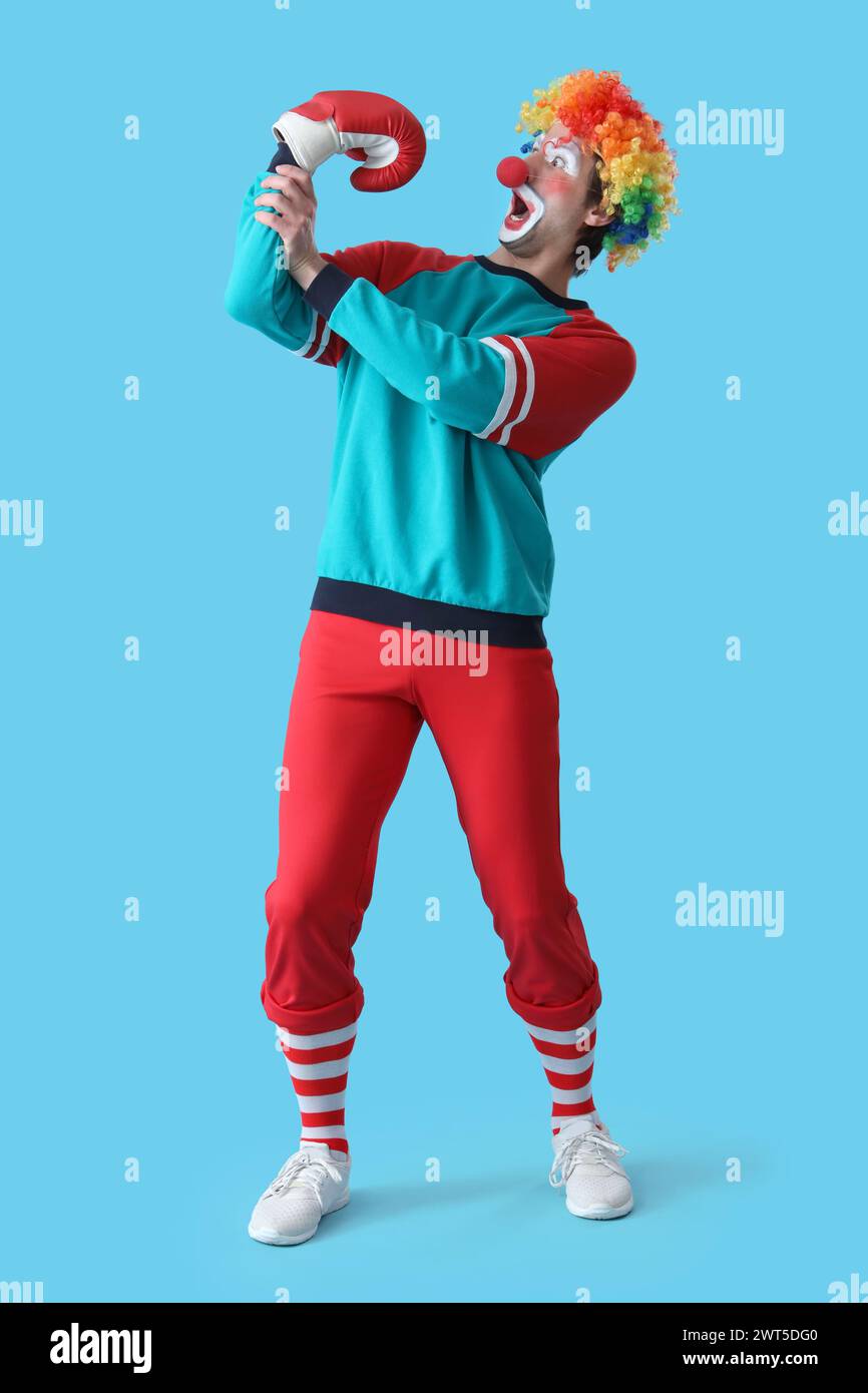 Portrait of surprised clown with boxing glove on blue background. April ...