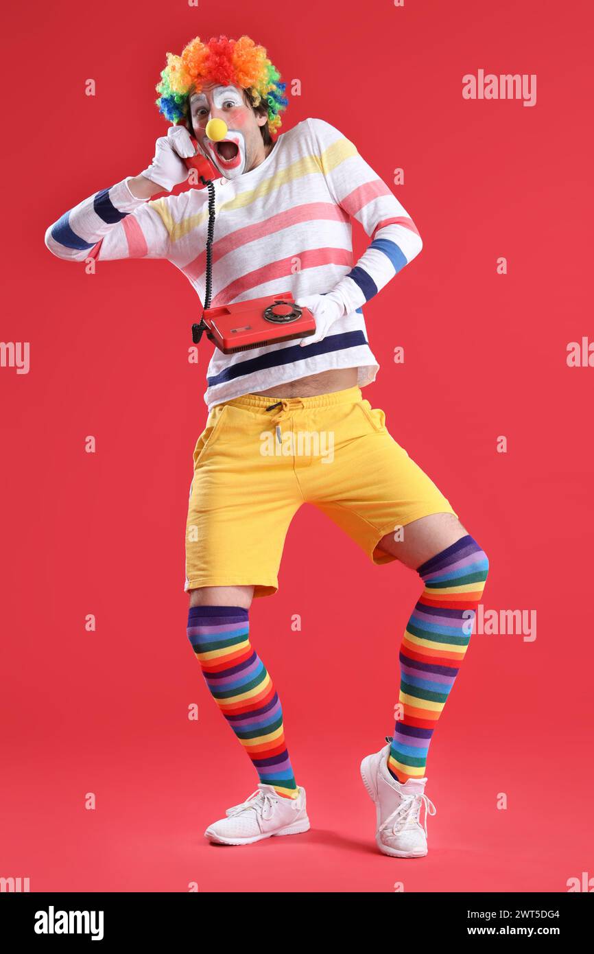 Portrait of surprised clown with retro telephone on red background ...