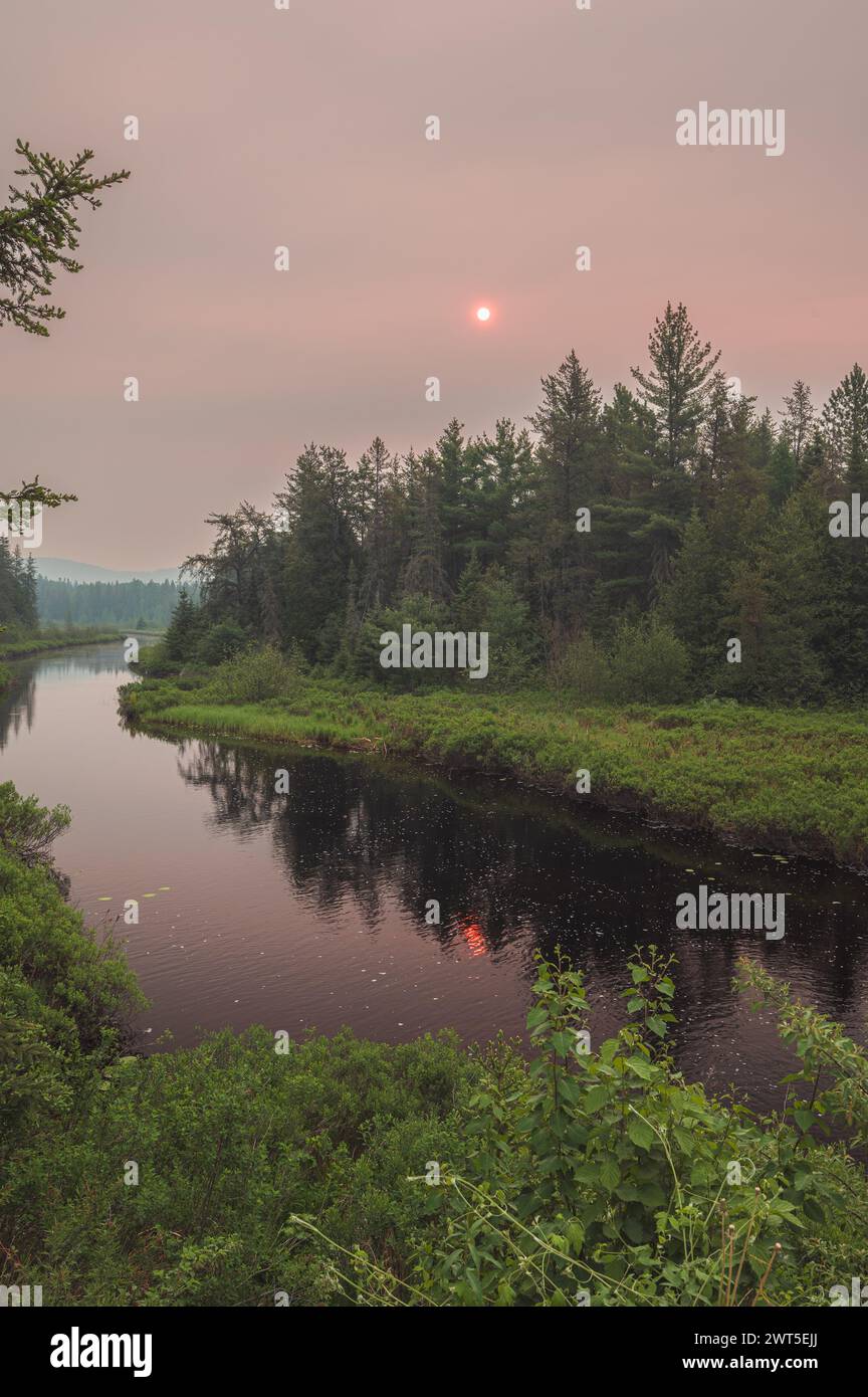 Forest fire smoke haze. Sunrise through smokey air with calm river ...