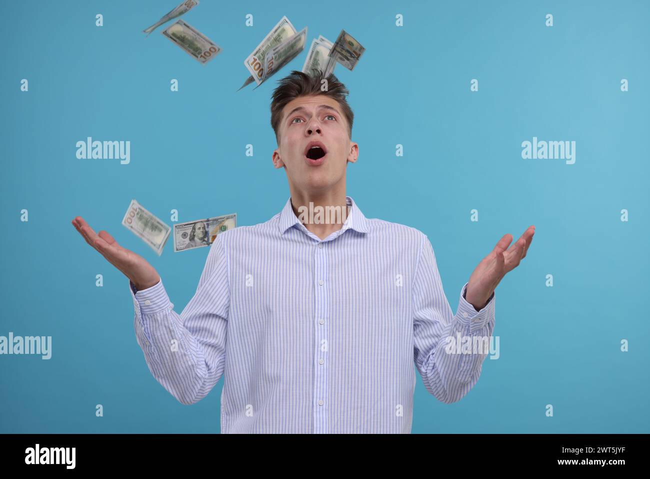Handsome man under money shower on light blue background Stock Photo ...