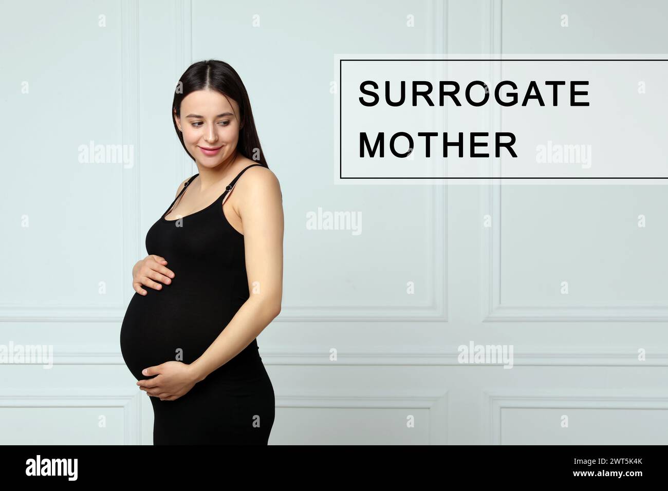 Surrogate mother. Pregnant woman touching her belly near white wall ...