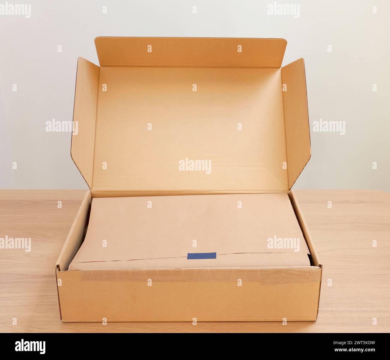 Open cardboard box with item wrapped in kraft paper on wooden table ...