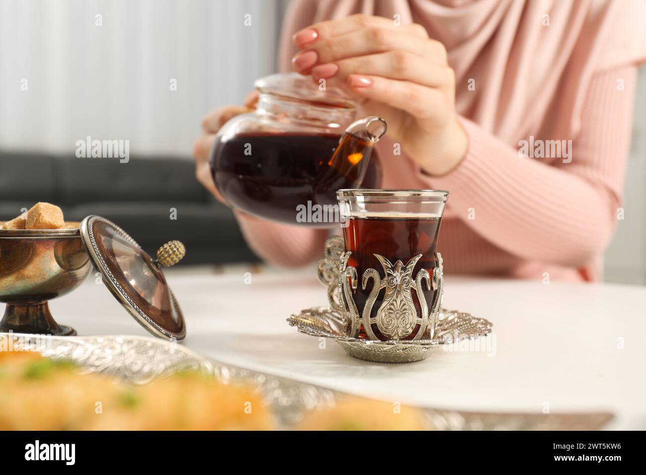 Woman pouring delicious Turkish tea from teapot into cup at white table ...