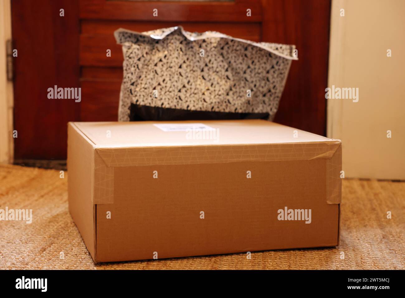 Delivery service. Plastic bag and cardboard on rug indoors Stock Photo ...