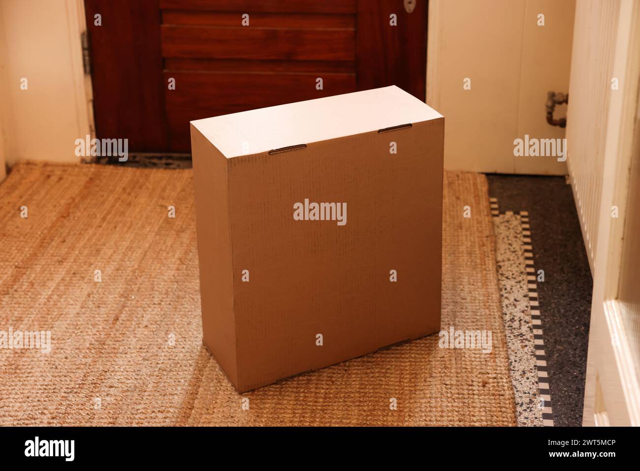 Delivery service. Cardboard on rug near wooden door indoors Stock Photo ...