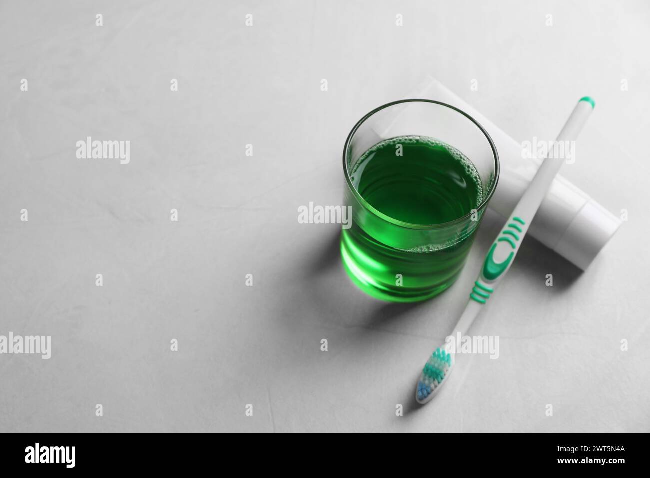 Fresh mouthwash in glass, toothpaste and toothbrush on light background ...