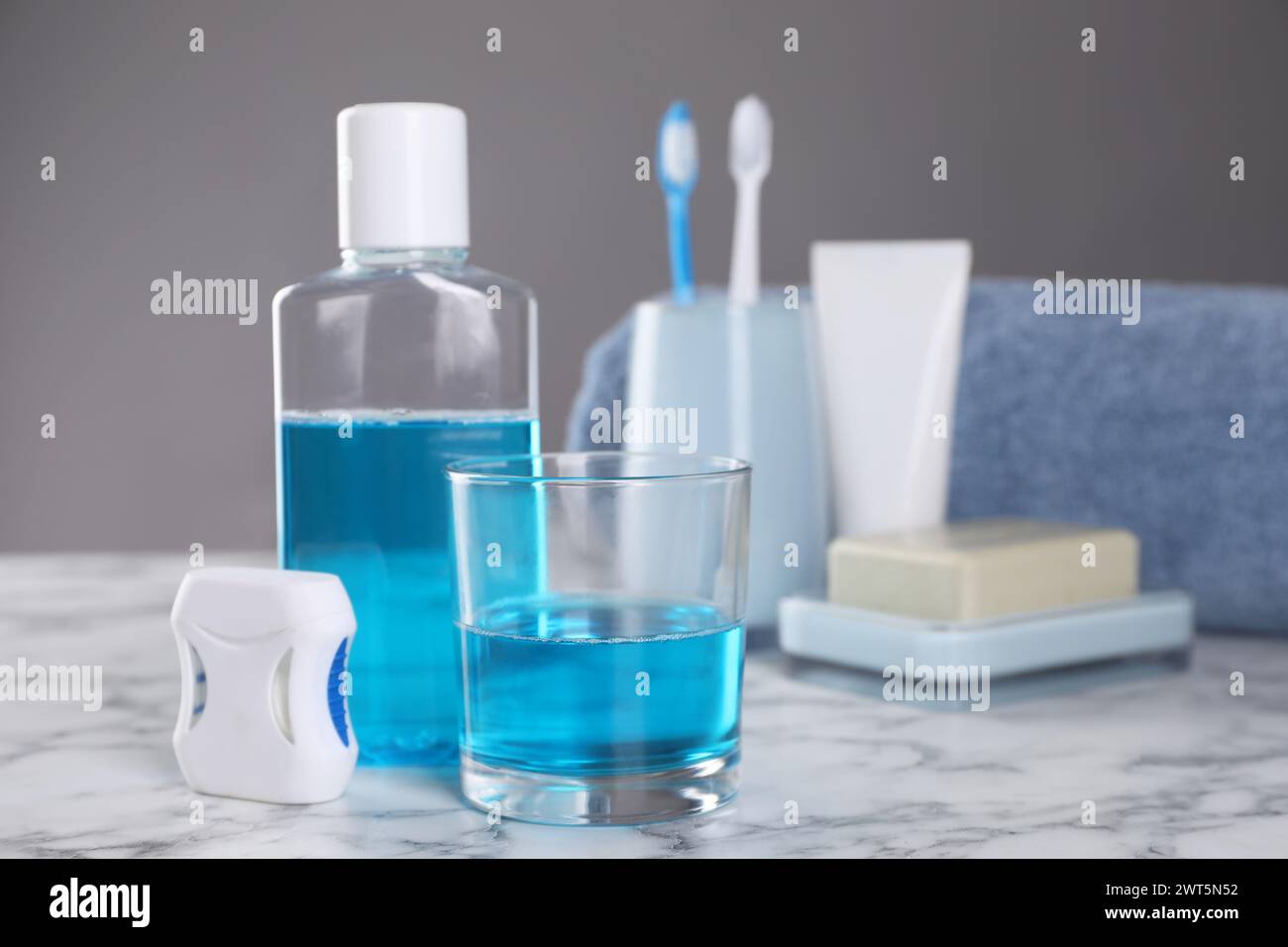 Fresh mouthwash in bottle, glass and dental floss on white marble table ...