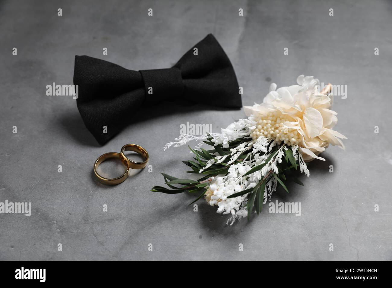 Wedding stuff. Stylish boutonniere, bow tie and wedding rings on gray ...