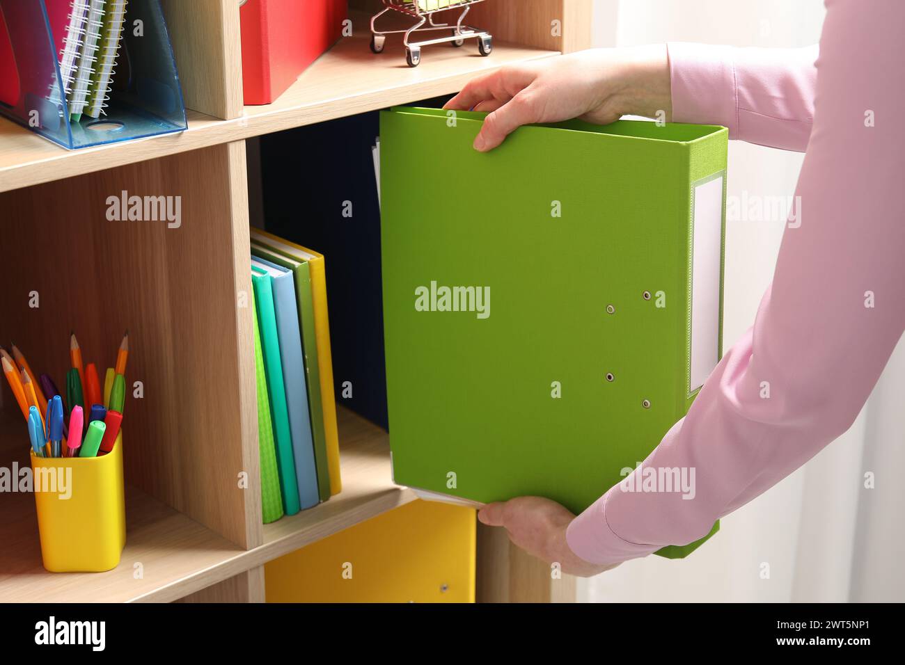 Woman taking binder office folder from shelving unit indoors, closeup ...
