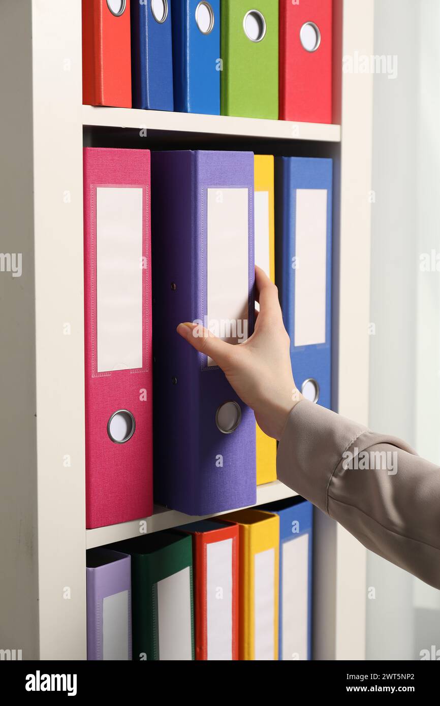 Woman taking binder office folder from shelving unit indoors, closeup ...