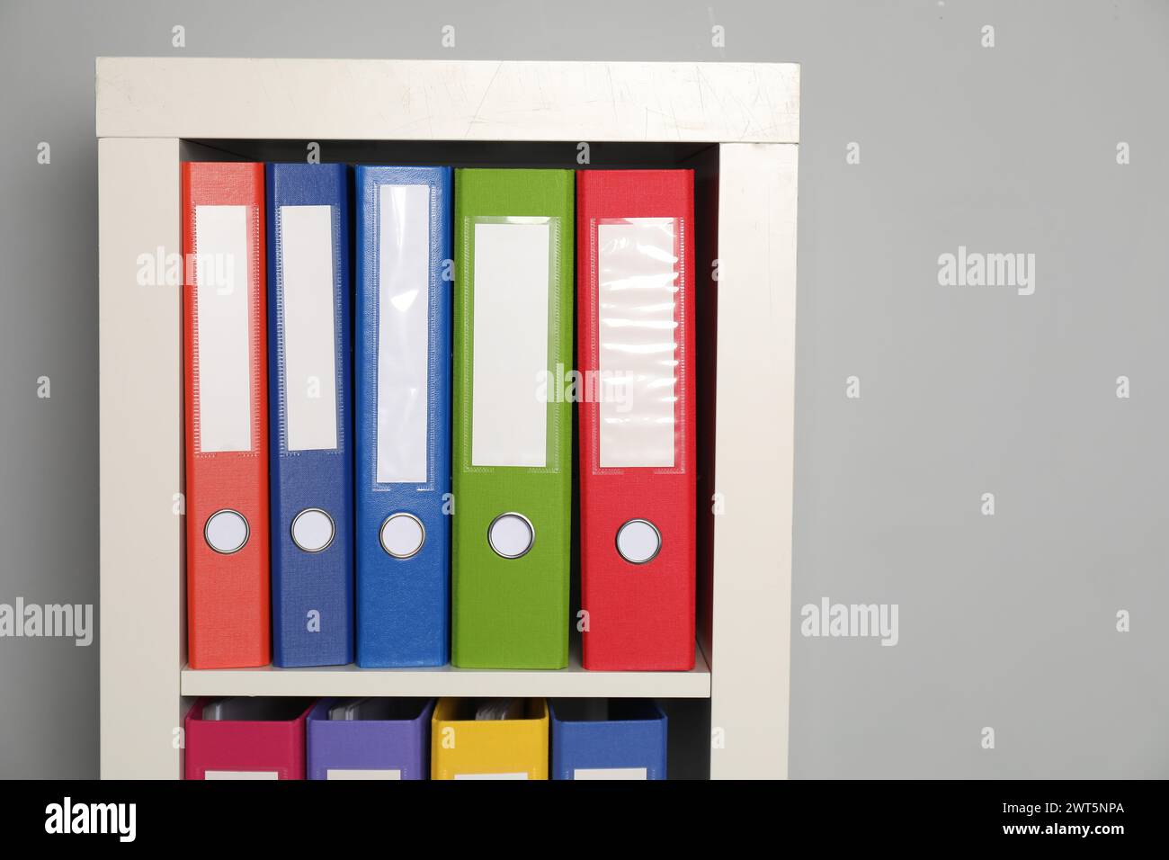 Colorful binder office folders on shelving unit near light grey wall ...