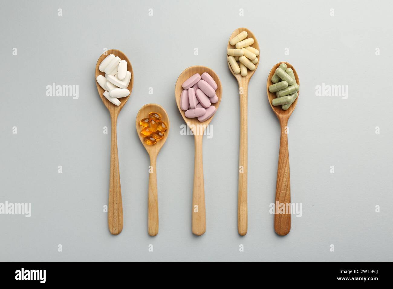 Different vitamin pills in spoons on light grey background, flat lay ...