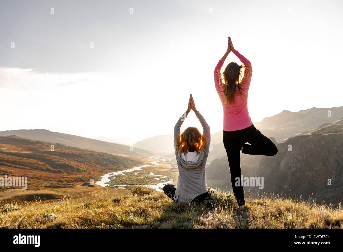 Two young women are relaxing in yoga poses at sunset mountains and ...