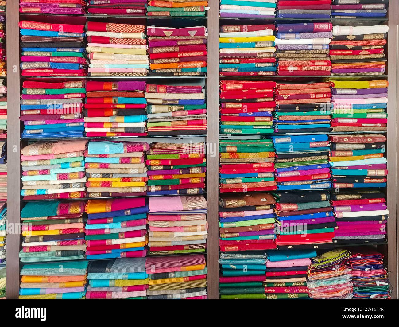 Neatly stacked colorful designer silk saris in racks in a textile shop ...