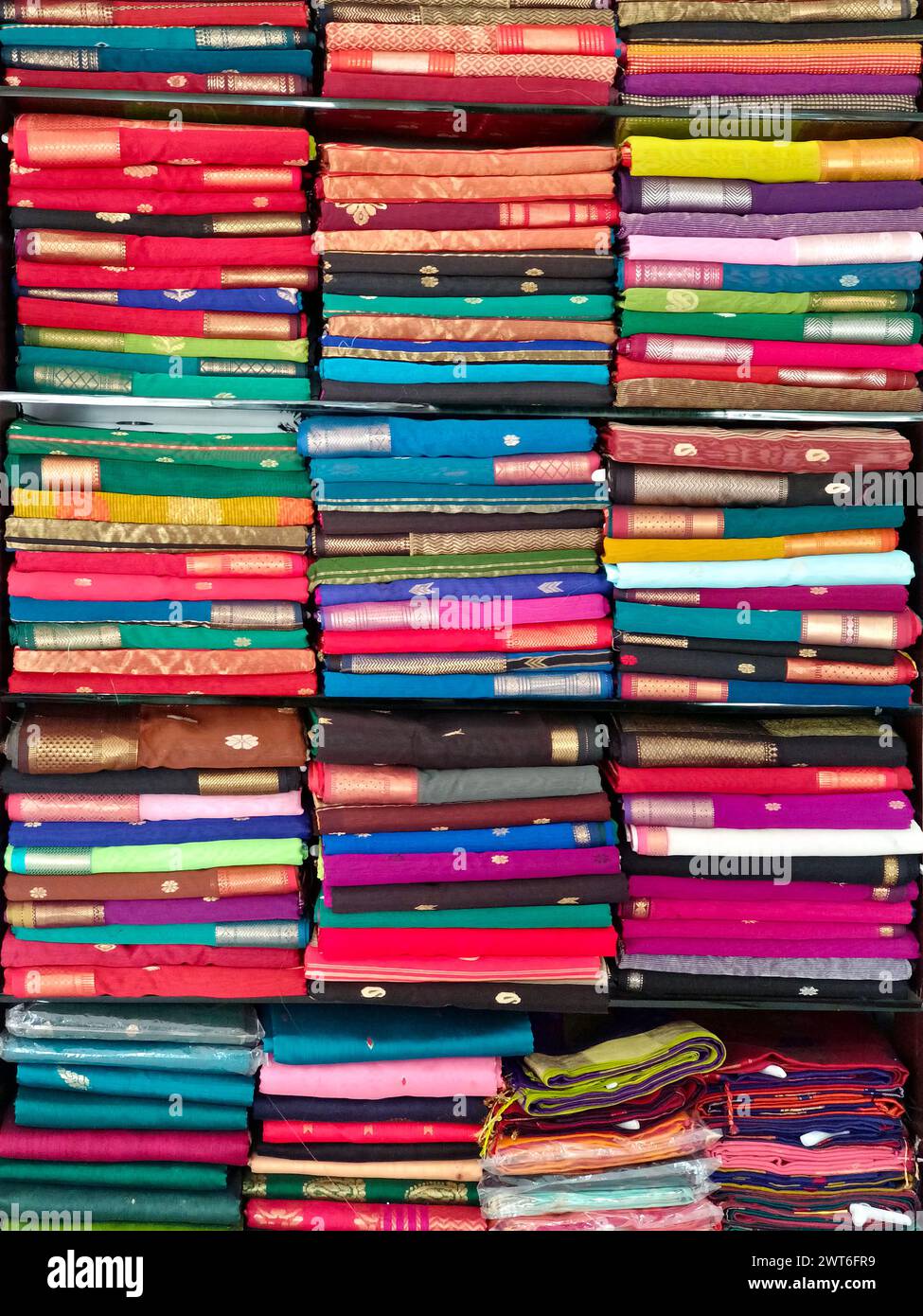 Neatly stacked colorful designer silk saris in racks in a textile shop ...
