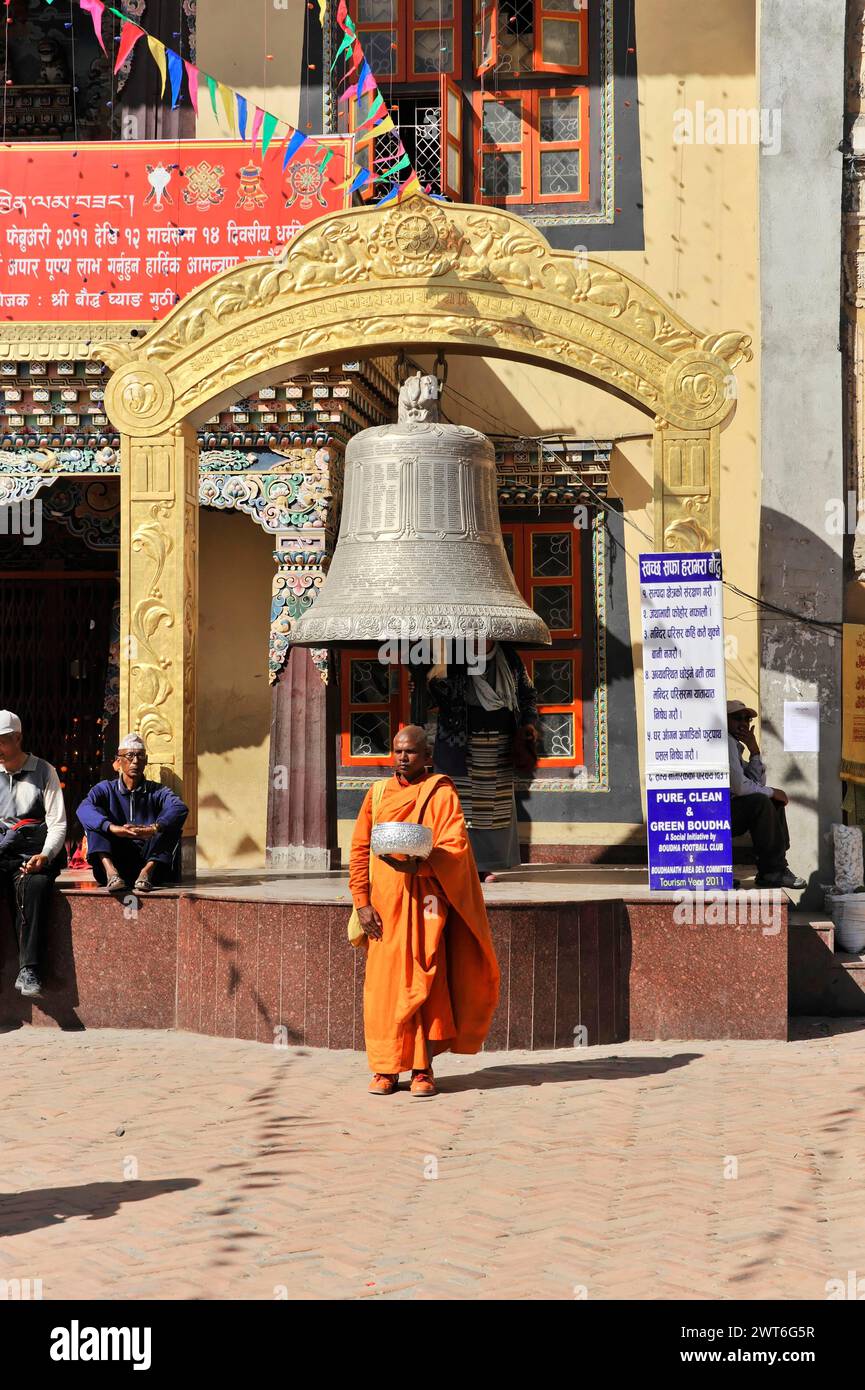 A monk stands in front of a large bell at a temple with colourful flags ...