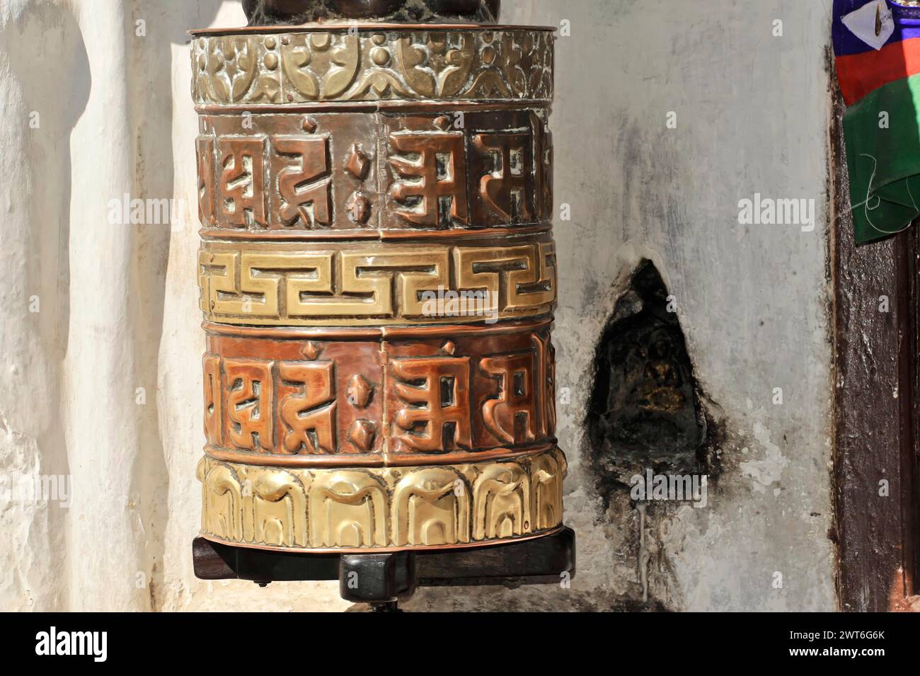 A golden prayer wheel with carvings stands in front of a wall ...