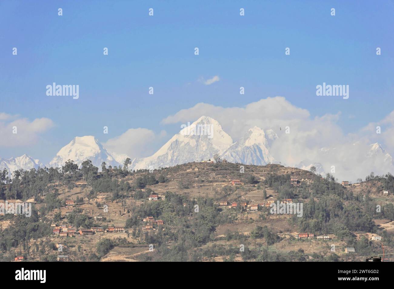 Snow-capped mountains tower over a rural settlement under a clear sky ...