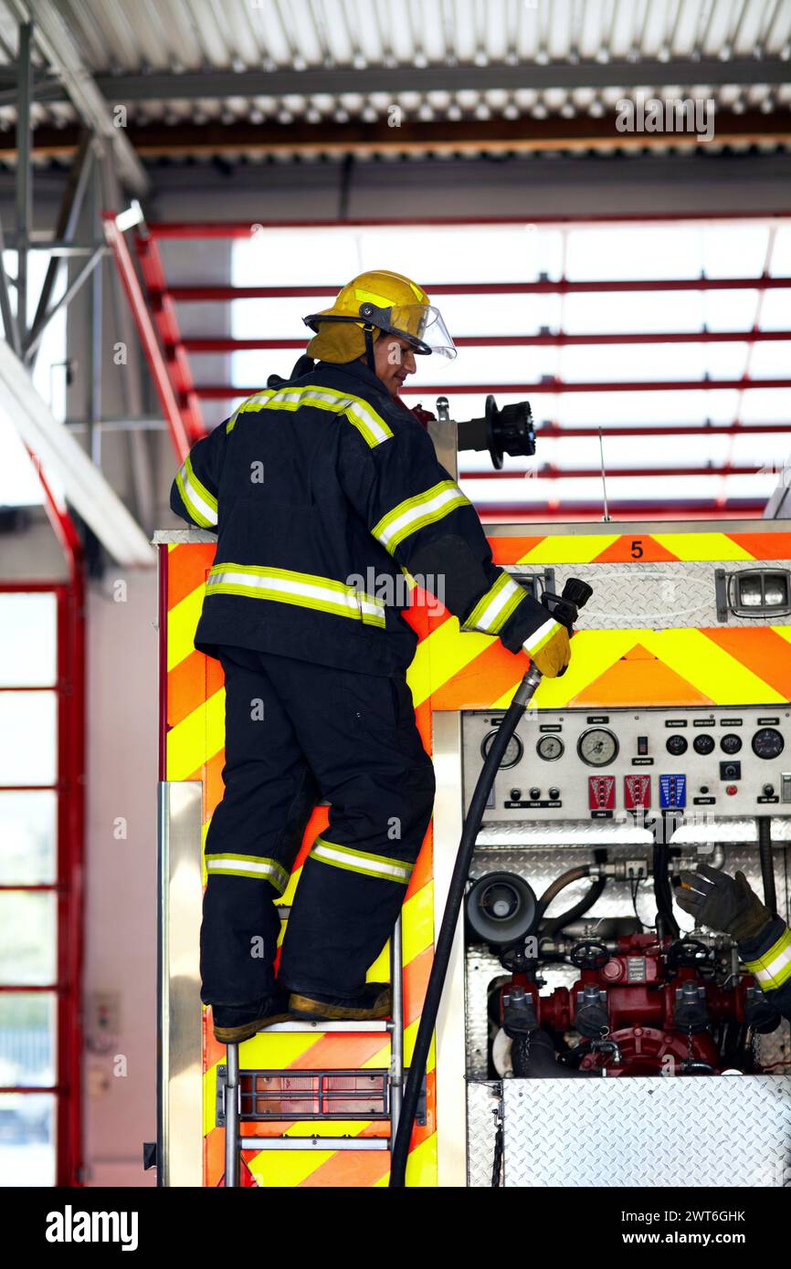 Firefighter, ladder and safety worker with hose truck at a fire station ...