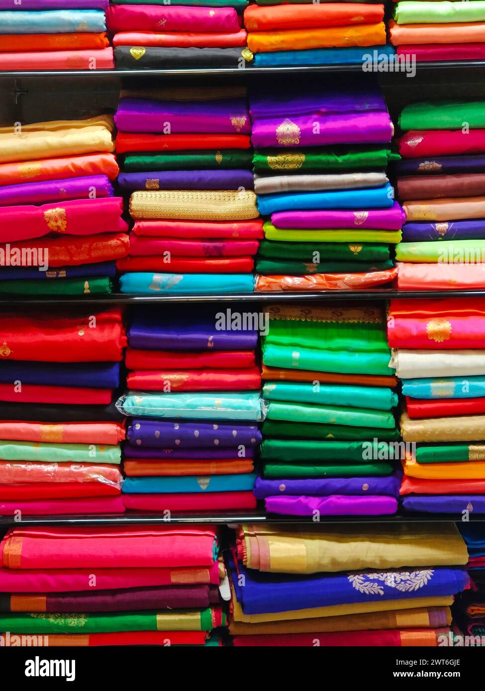 Neatly stacked colorful designer silk saris in racks in a textile shop ...