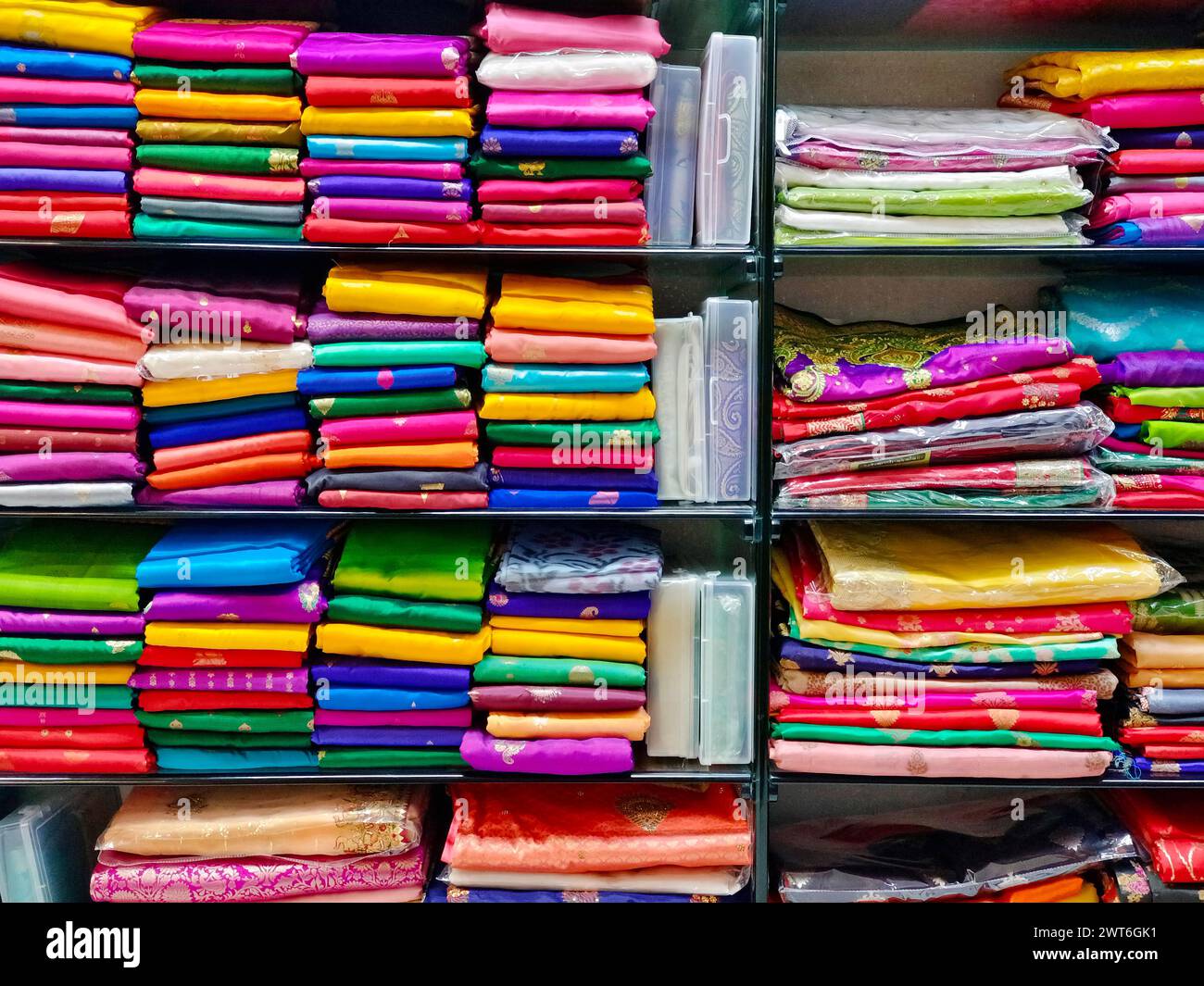 Neatly stacked colorful designer silk saris in racks in a textile shop ...