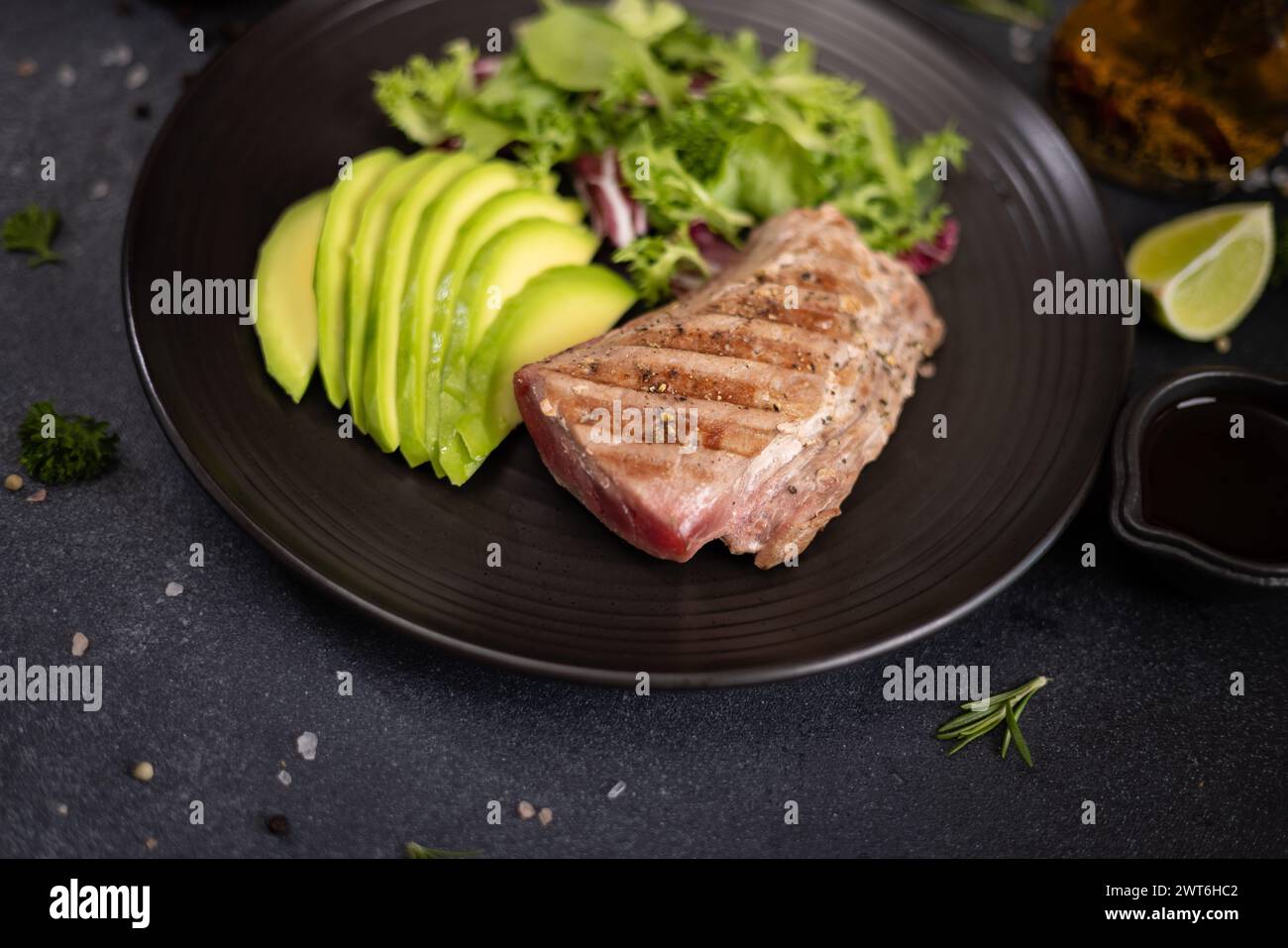 grilled cooked piece of tuna fillet with sliced avocado and salad on ...