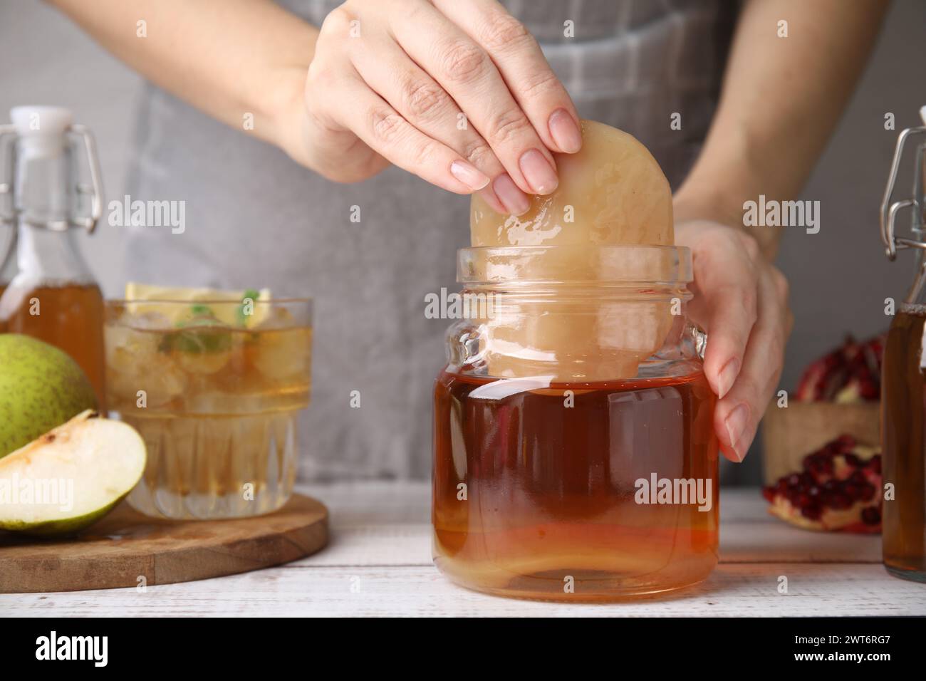 Woman putting Scoby fungus into jar with kombucha at white wooden table ...