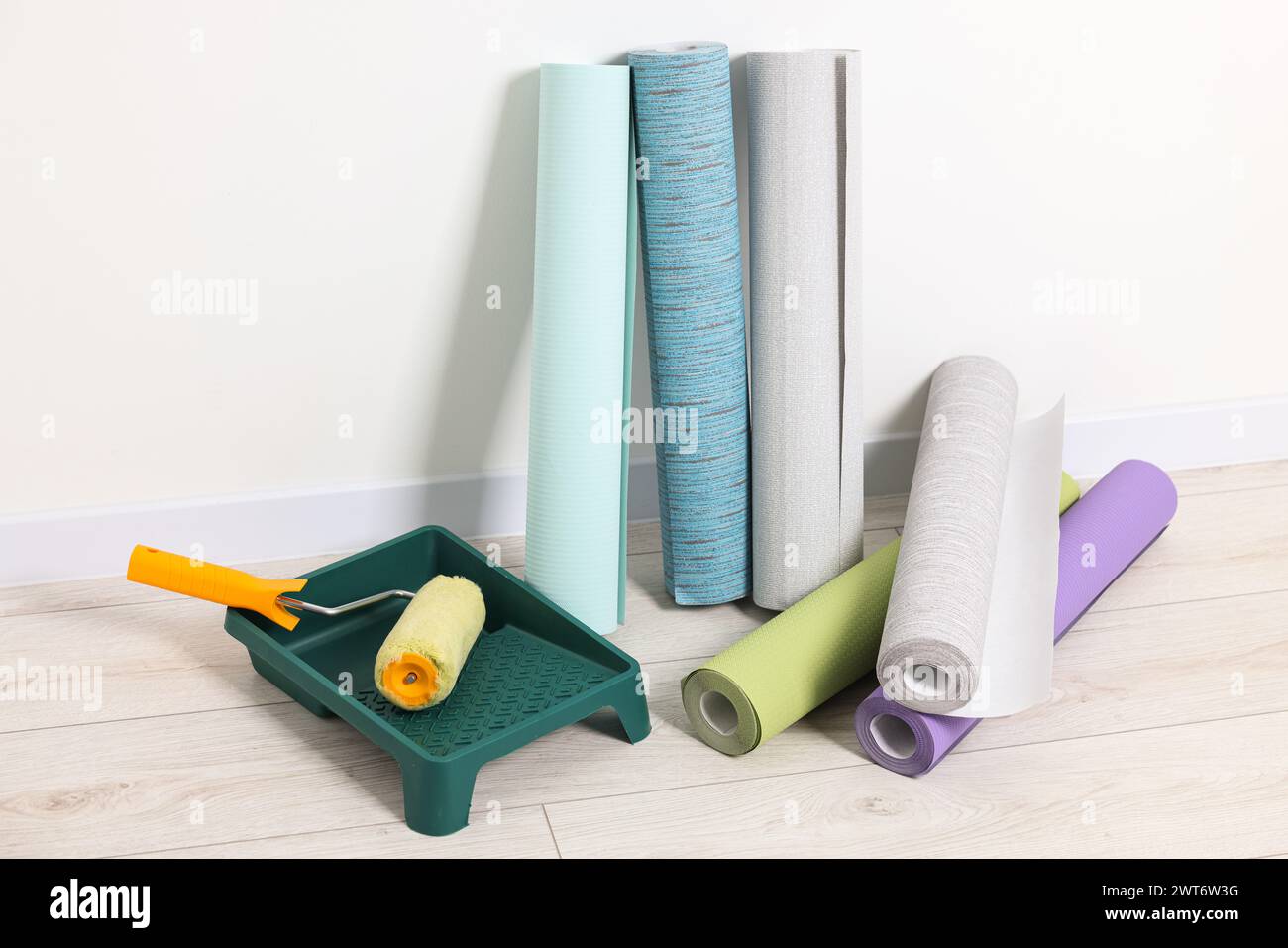 Different wallpaper rolls, roller and tray near white wall indoors ...