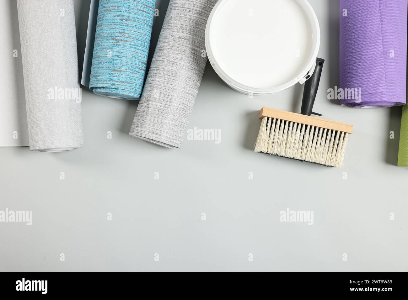 Different wallpaper rolls, brush and bucket with glue on light grey ...