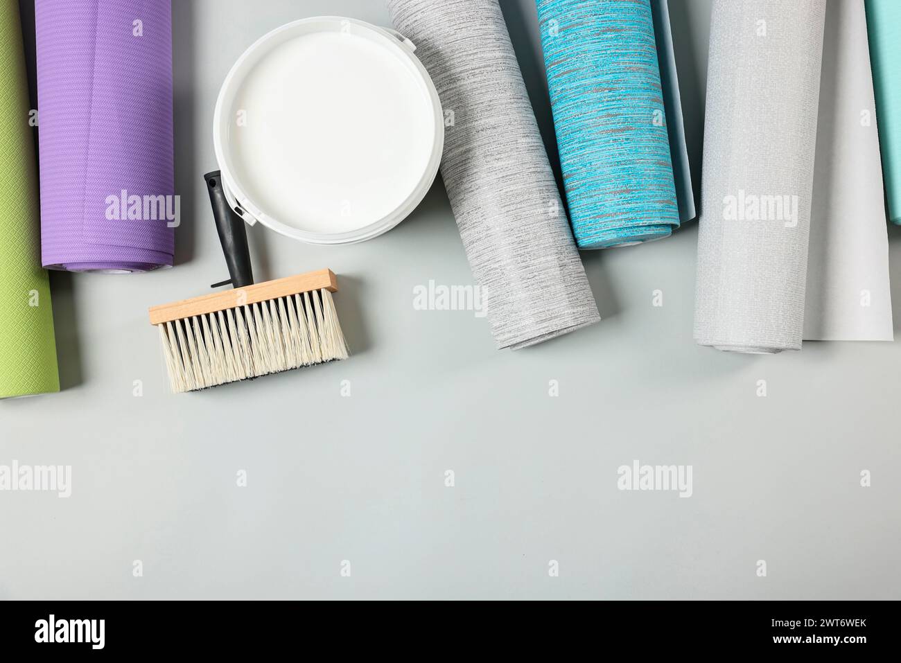 Different wallpaper rolls, brush and bucket with glue on light grey ...