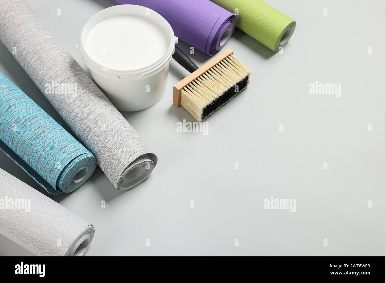 Different wallpaper rolls, brush and bucket with glue on light grey ...