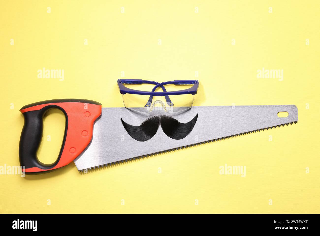 Man's face made of artificial mustache, safety glasses and hand saw on ...