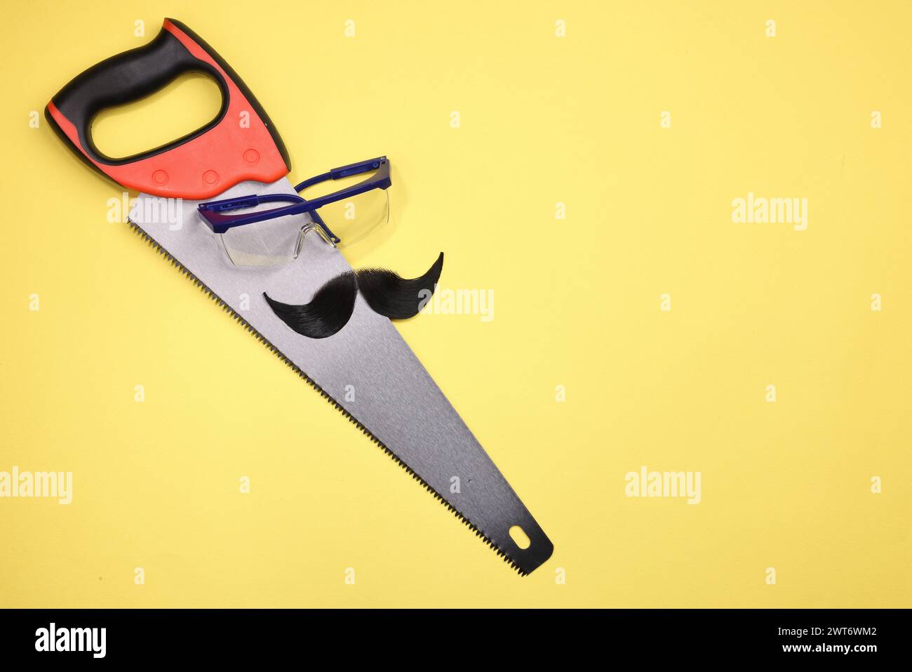 Man's face made of artificial mustache, safety glasses and hand saw on ...