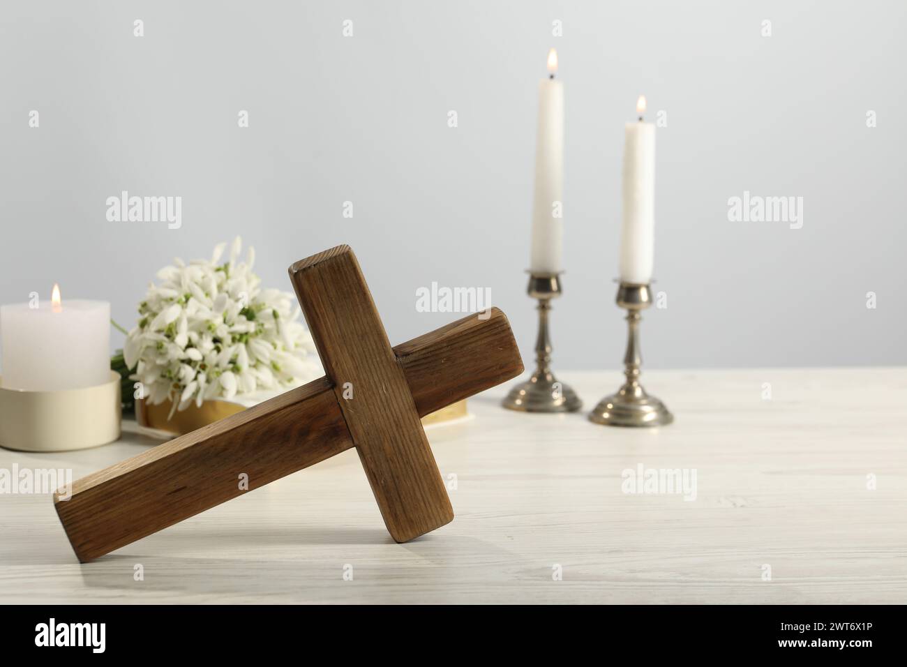 Burning church candles, wooden cross and flowers on white table. Space ...