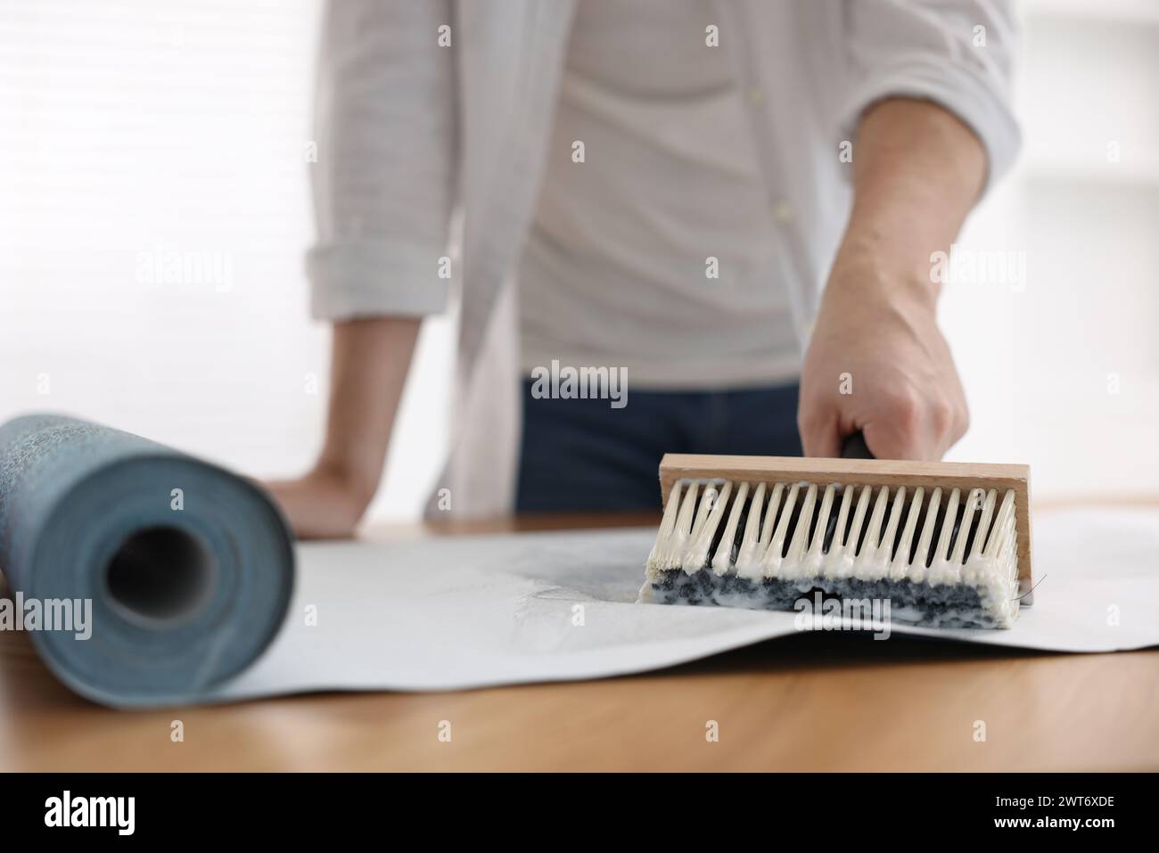 Man applying glue onto wallpaper sheet at table indoors, closeup Stock ...