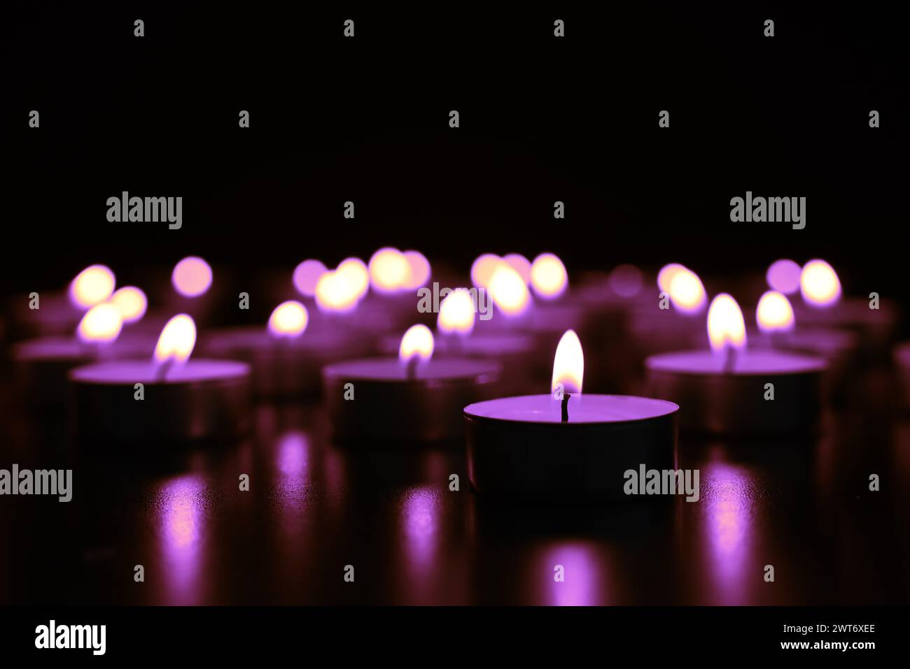 Burning violet candle on black background, closeup. Funeral attributes ...
