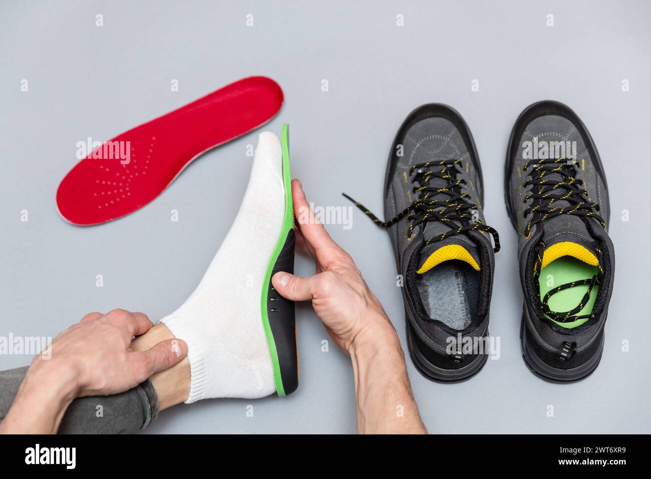 Close up of man hands fitting orthopedic insoles on a gray background ...
