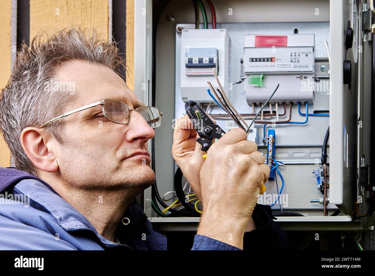 An electrician strips insulation from wire of three-phase power cable ...