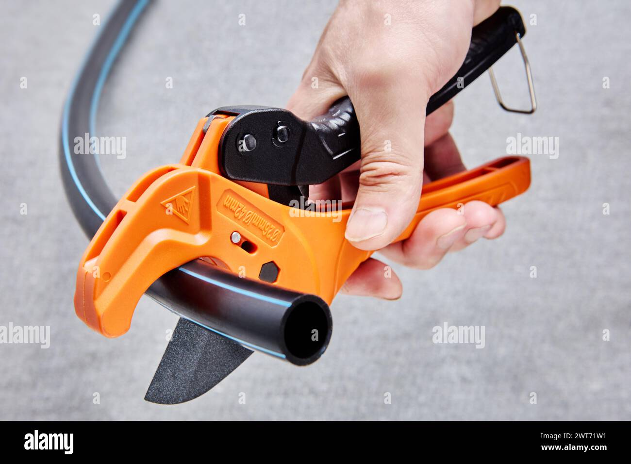 Orange ratcheting PVC pipe cutter tool in hand of plumber cutting off ...