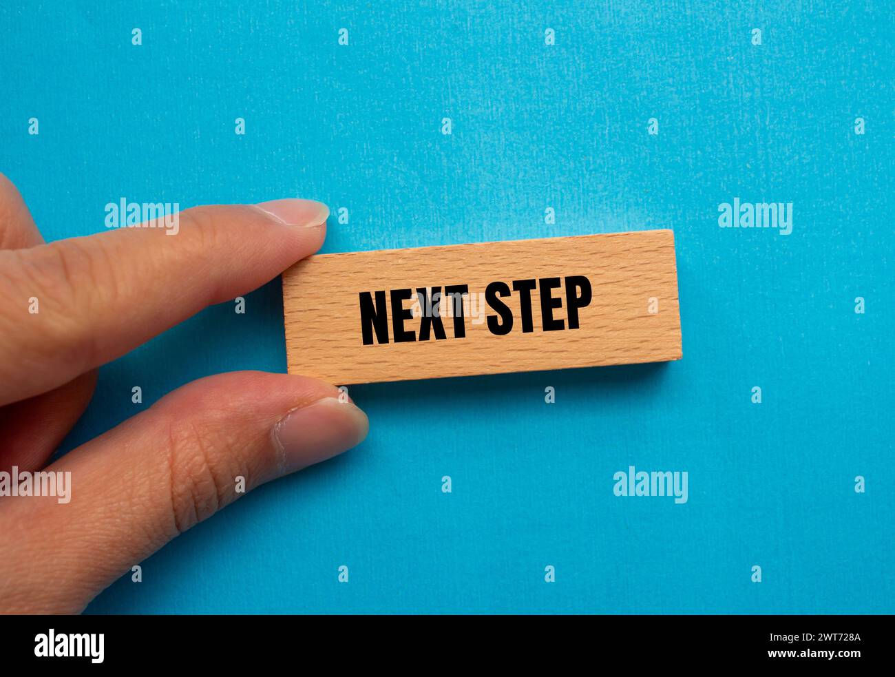 Next step words written on torn wooden block with blue background ...