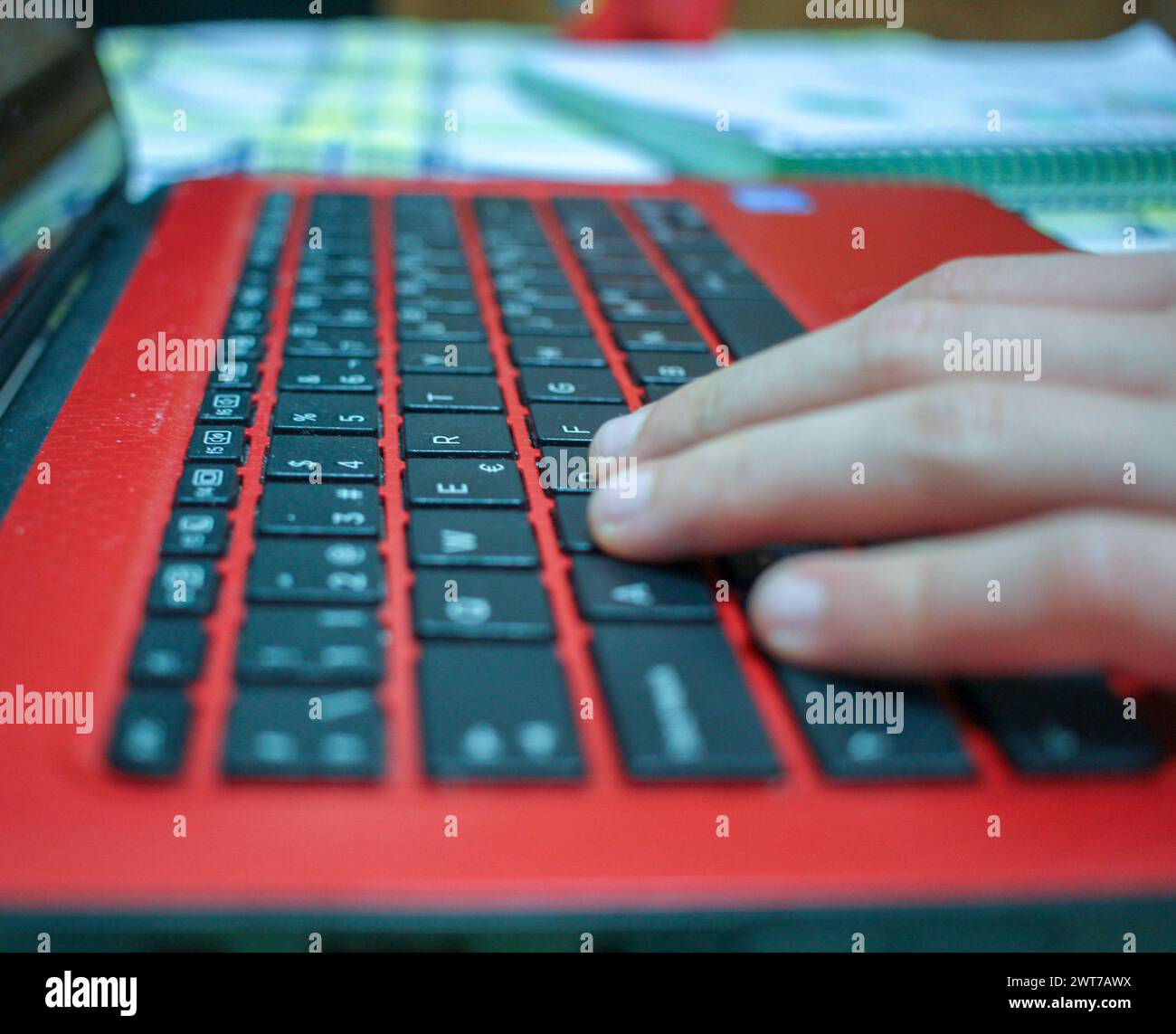 a boy is pressing the keys of a red laptop to do his homework Stock ...