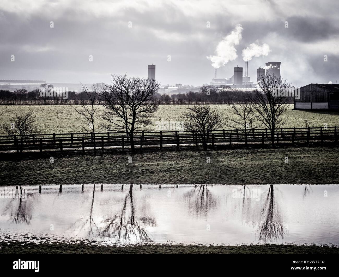 Trees reflect in a water logged field, power stations can be seen in ...
