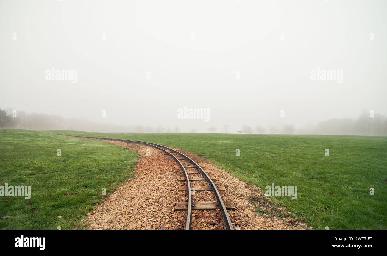 Narrow gauge railway in the foggy green field. The track curves away from the viewer to the left ...