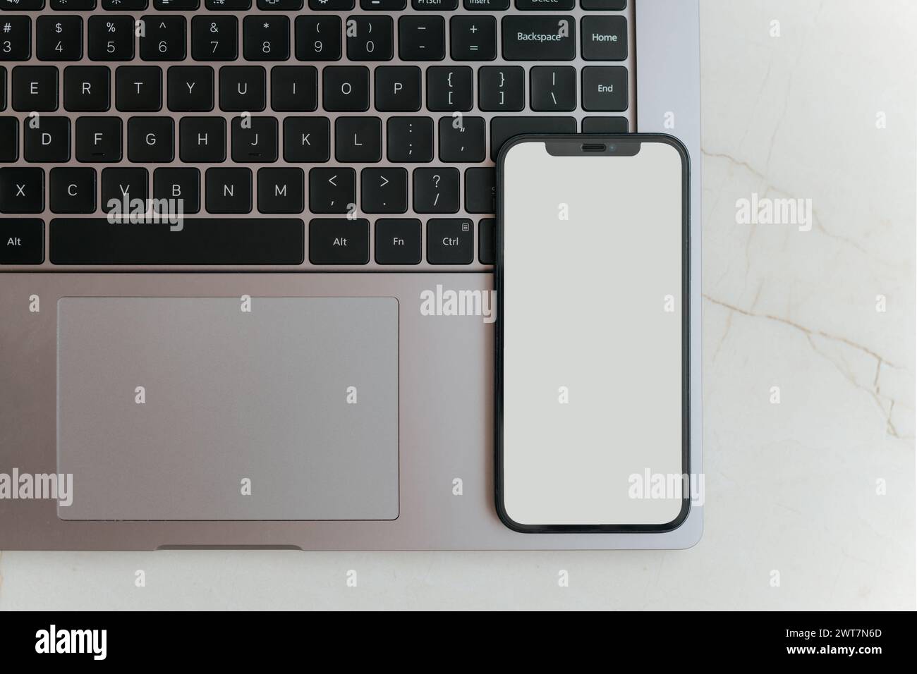 Mobile phone with blank screen lying on laptop keyboard. Top view, flat ...