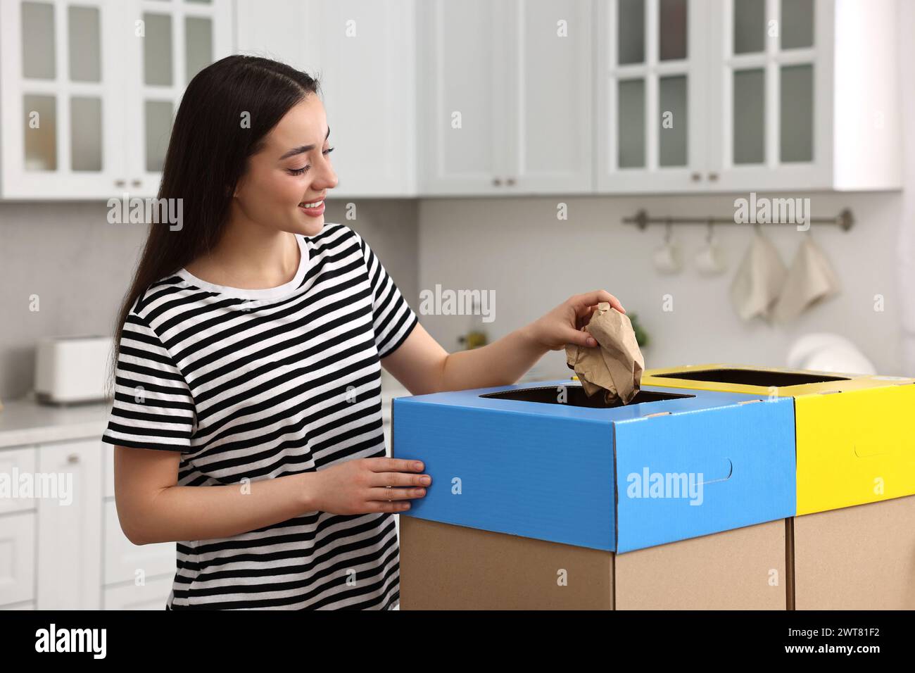 Garbage sorting. Smiling woman throwing crumpled paper into cardboard ...