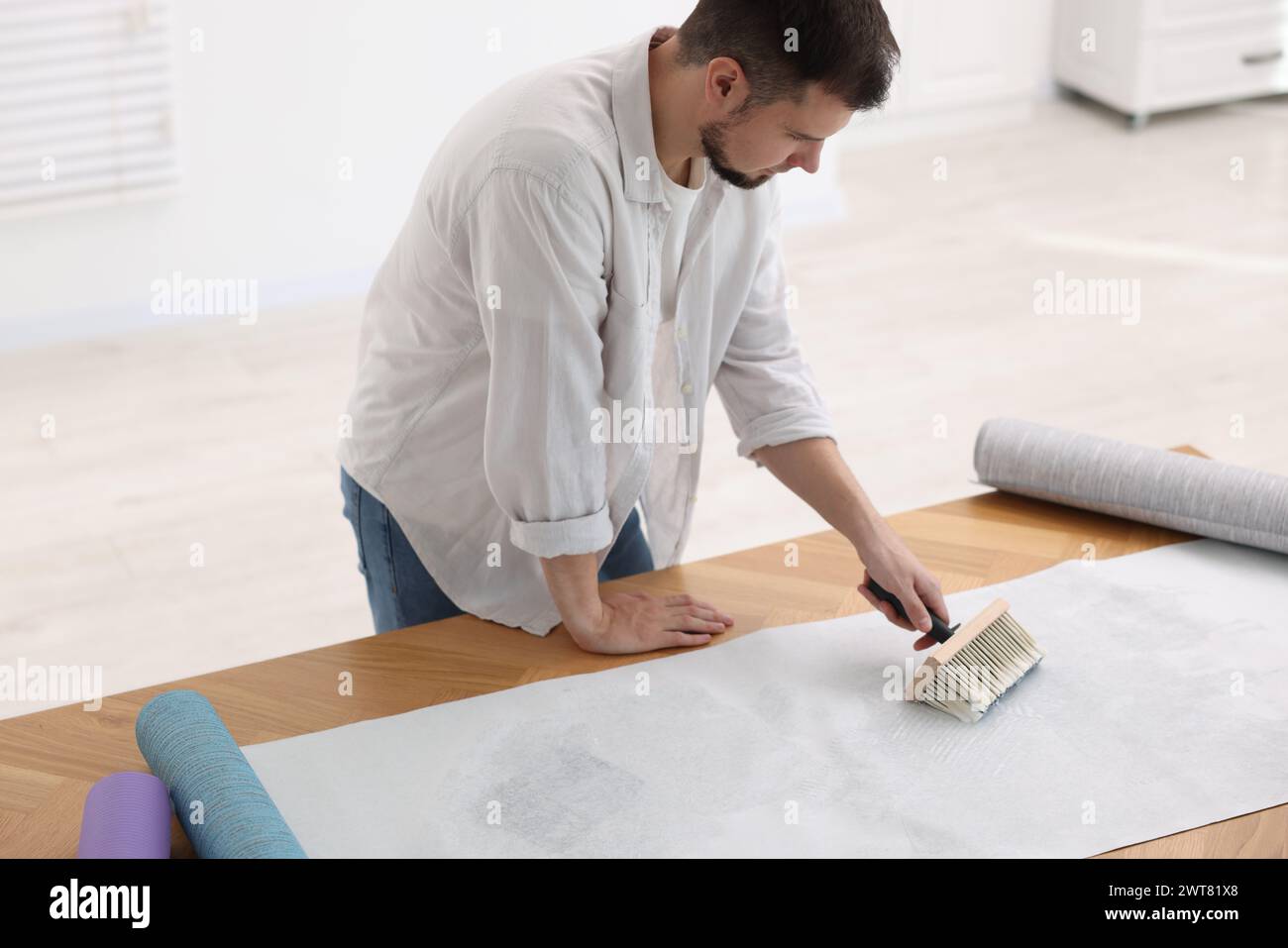 Man applying glue onto wallpaper sheet at wooden table indoors Stock ...