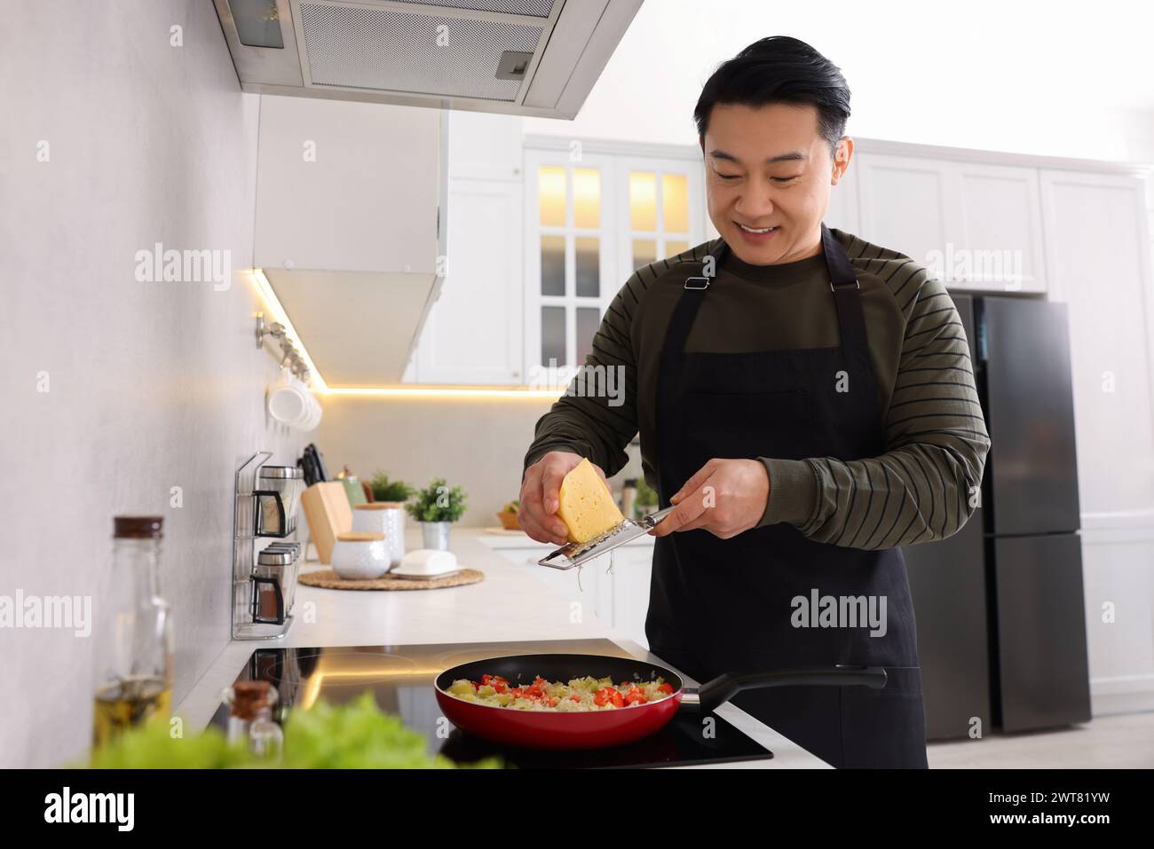Cooking process. Man grating cheese into frying pan in kitchen Stock ...